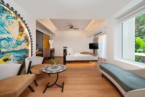 Quarto de hotel moderno com cama, sofá, pequena mesa com planta e uma grande janela com vista para área verde.