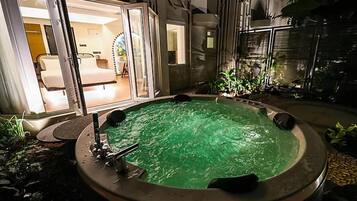 Uma banheira de hidromassagem com formato circular e água esverdeada, rodeada por plantas e pedras.
