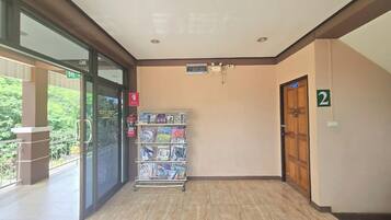 Um hall de hotel com uma recepção, um relógio digital, um extintor de incêndio e uma porta marcada com o número 2.