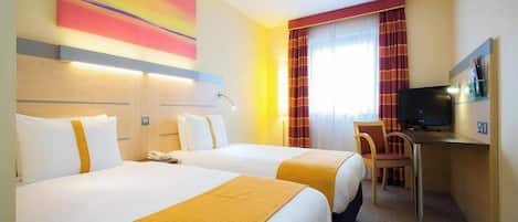 Quarto de hotel com duas camas, uma mesa de trabalho e uma televisão, além de uma janela com cortinas.