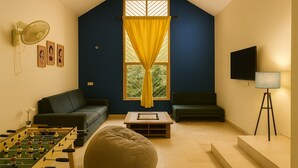Uma sala de estar aconchegante com uma parede de destaque azul escuro, uma cortina amarela, um sofá, uma mesa de centro, uma TV e uma mesa de pebolim.