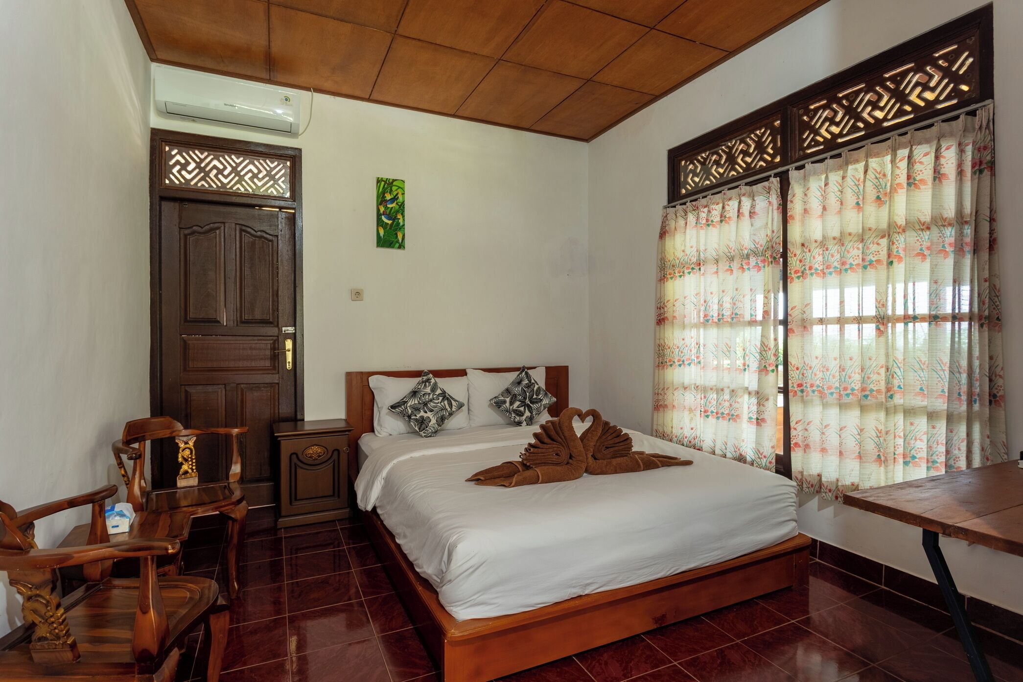 Um quarto bem arrumado com uma cama e mesa de cabeceira de madeira, uma cadeira, uma mesa e um objeto decorativo na parede.