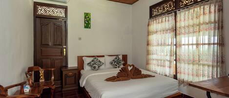 Um quarto bem arrumado com uma cama e mesa de cabeceira de madeira, uma cadeira, uma mesa e um objeto decorativo na parede.