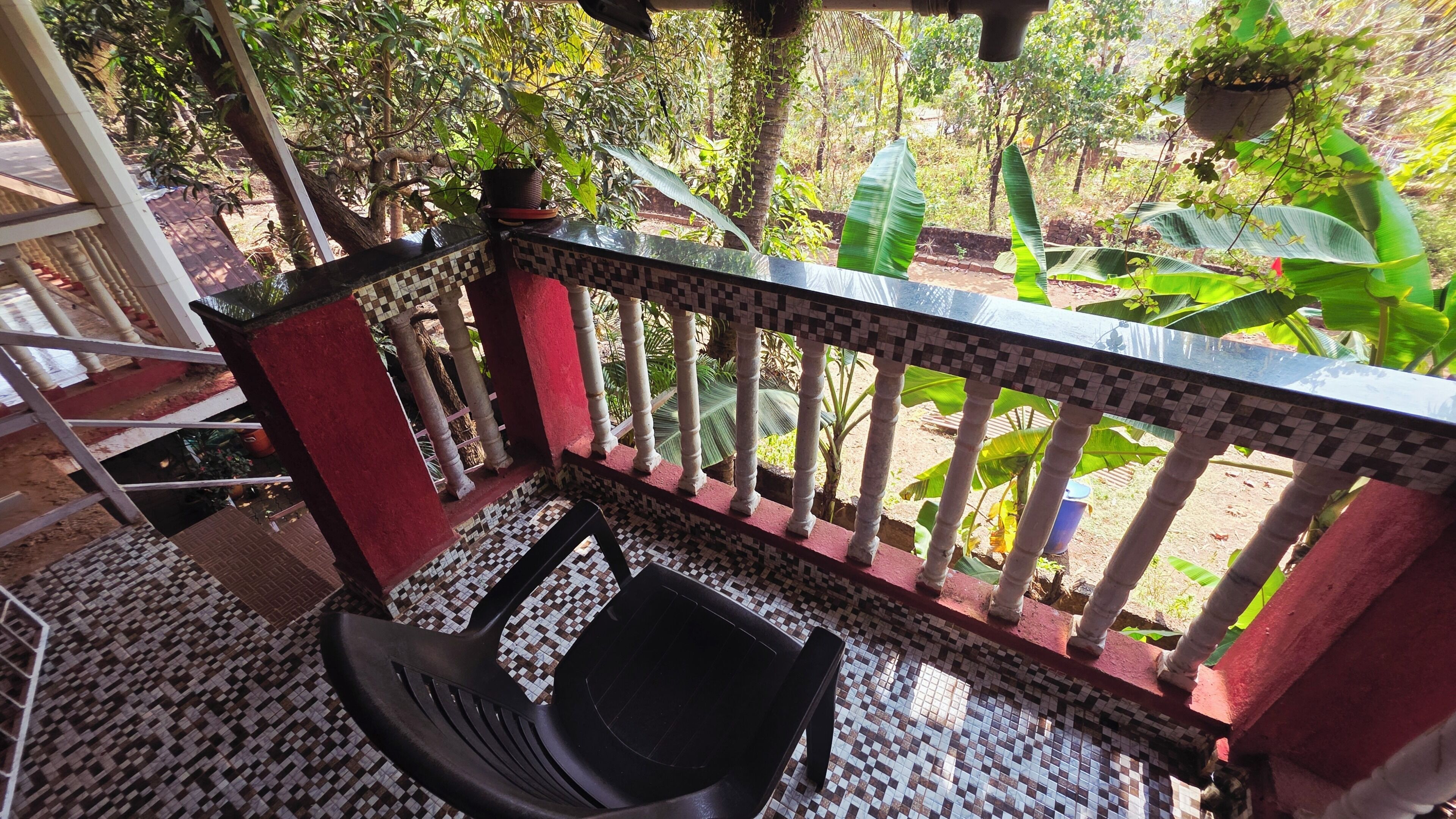 Uma varanda com uma cadeira de plástico preta, piso de azulejos e vista para o verde.