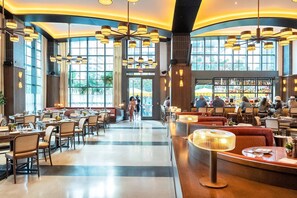Um hall de hotel espaçoso com área de bar, assentos e amplas janelas que permitem a entrada de luz natural.