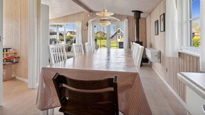 Uma sala de jantar com uma mesa grande, cadeiras brancas e vista para o exterior.