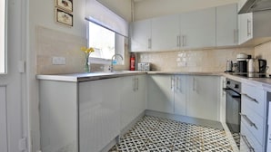 Uma cozinha moderna com armários brancos, piso de azulejos estampados, janela com persianas e uma cafeteira.