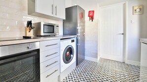 Uma cozinha moderna com armários brancos, uma geladeira de aço inoxidável, micro-ondas, forno embutido e máquina de lavar.