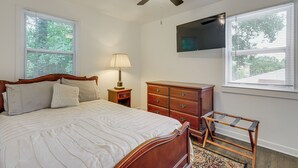Quarto com cama, cômoda, mesa de cabeceira, luminária, ventilador de teto e televisão na parede.