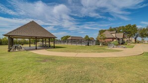 Um parque com mesas de piquenique, um coreto e uma área cercada com casas ao fundo.