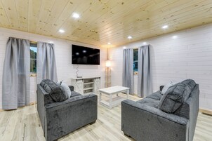 Um quarto aconchegante com dois sofás cinzas, um rack branco para TV e uma mesa pequena branca.