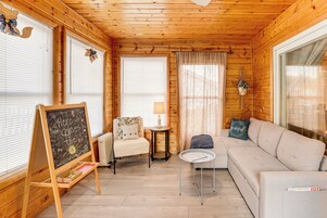 Interior acolhedor de uma cabana com teto de madeira, uma lousa com escrita, um sofá, uma poltrona e uma pequena mesa.