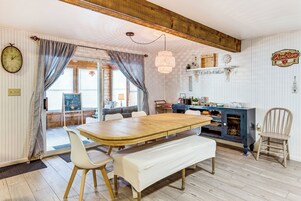 Uma área de refeições com mesa de madeira, banco branco e cadeiras. Há um armário azul com uma prateleira acima da mesa.