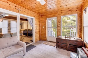 Interior acolhedor de uma cabana com teto de madeira, um sofá, uma cômoda e uma janela grande com vista para o exterior.