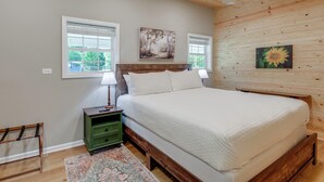 Quarto com cama de madeira, mesa de cabeceira, cômoda verde e duas janelas com persianas.