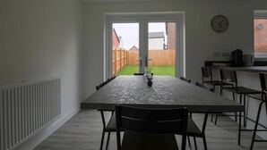 Uma sala de jantar com mesa e cadeiras, uma janela com relógio e vista para o quintal.