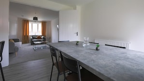 Uma cozinha moderna com bancada de mármore, sala de jantar com mesa e cadeiras, e sala de estar com sofá e janela com cortinas.