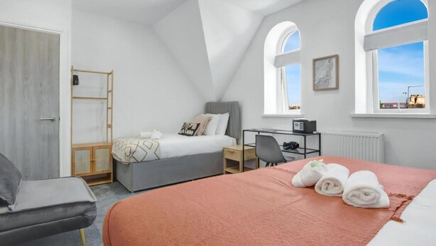 Quarto moderno com cama, escrivaninha e cadeira, guarda-roupa e janela com vista para a cidade.