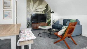 Uma sala de estar moderna com televisão, sofá, cadeira de madeira e uma mesa redonda pequena.