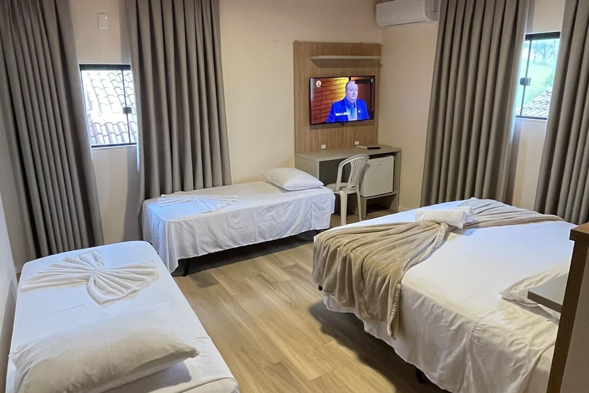 Quarto de hotel com duas camas de solteiro, uma televisão na parede e uma escrivaninha com uma cadeira.