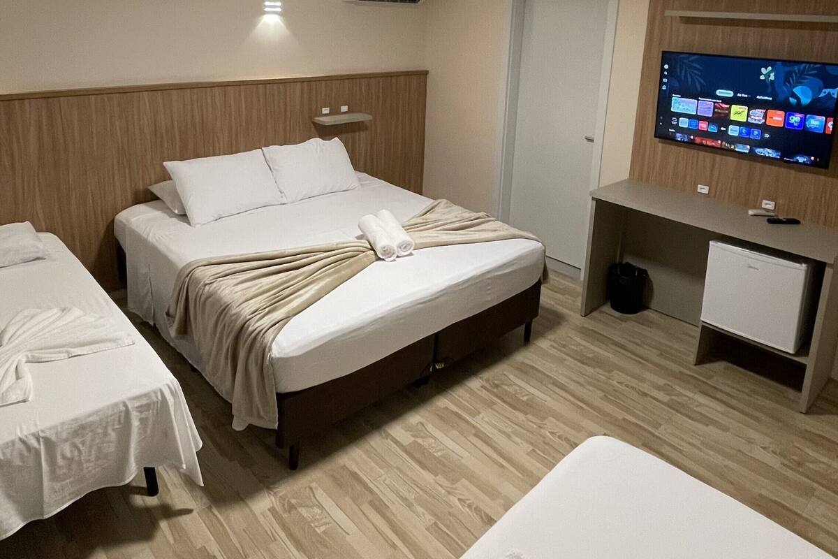 Quarto de hotel com duas camas, uma escrivaninha, televisão e ar condicionado.
