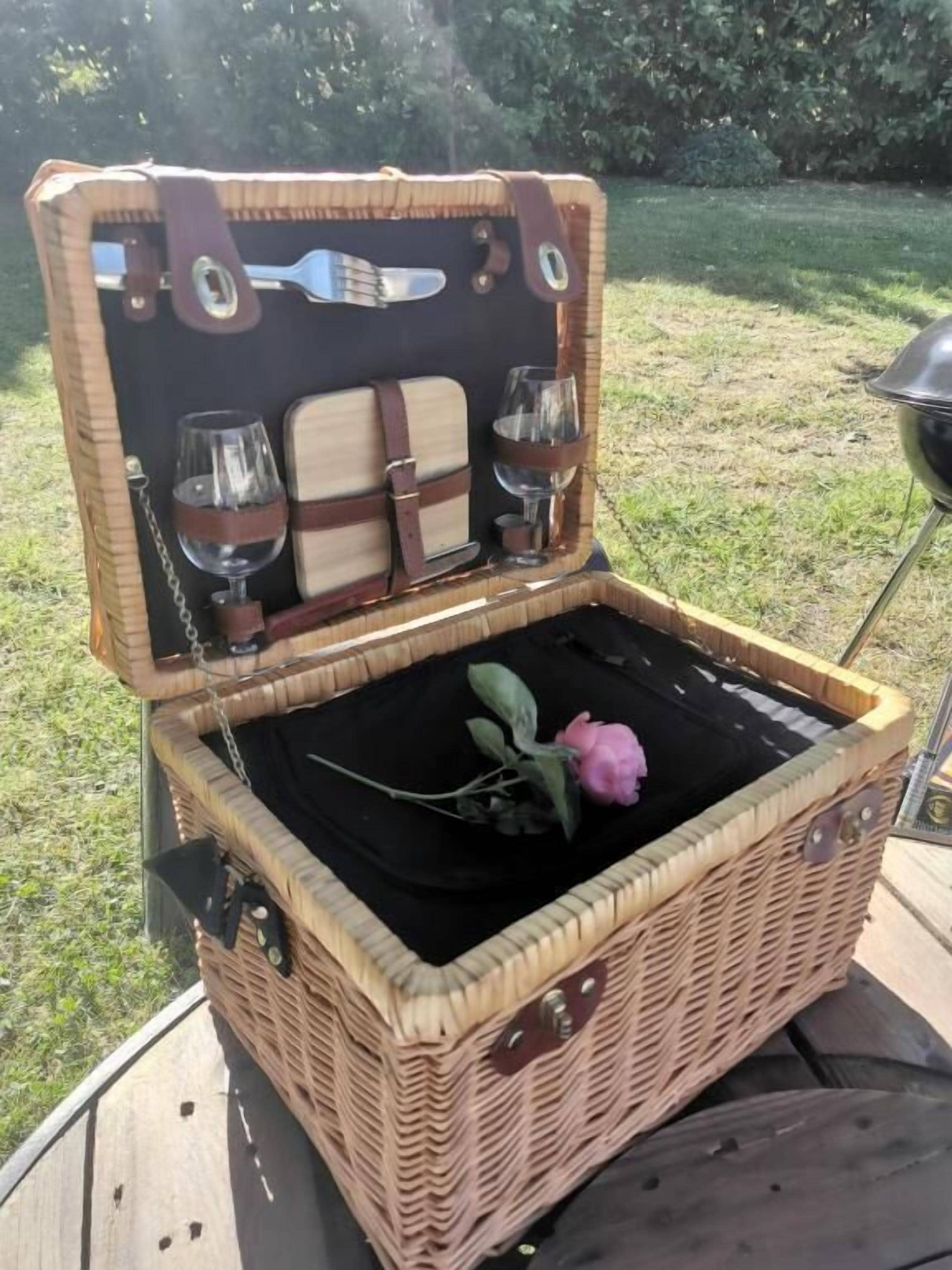 Uma cesta de piquenique de vime com interior preto, uma flor cor-de-rosa e uma taça de vinho.