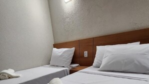 Quarto de hotel com duas camas, roupa de cama branca e uma toalha enrolada sobre a cama.