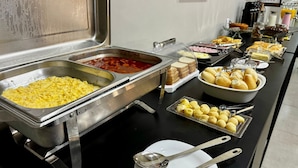 Buffet com diversos alimentos, incluindo ovos mexidos, feijão assado, pão e doces.