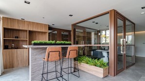 Uma cozinha moderna com armários de madeira, bancada de mármore, dois banquetes e uma área de refeições com paredes de vidro.