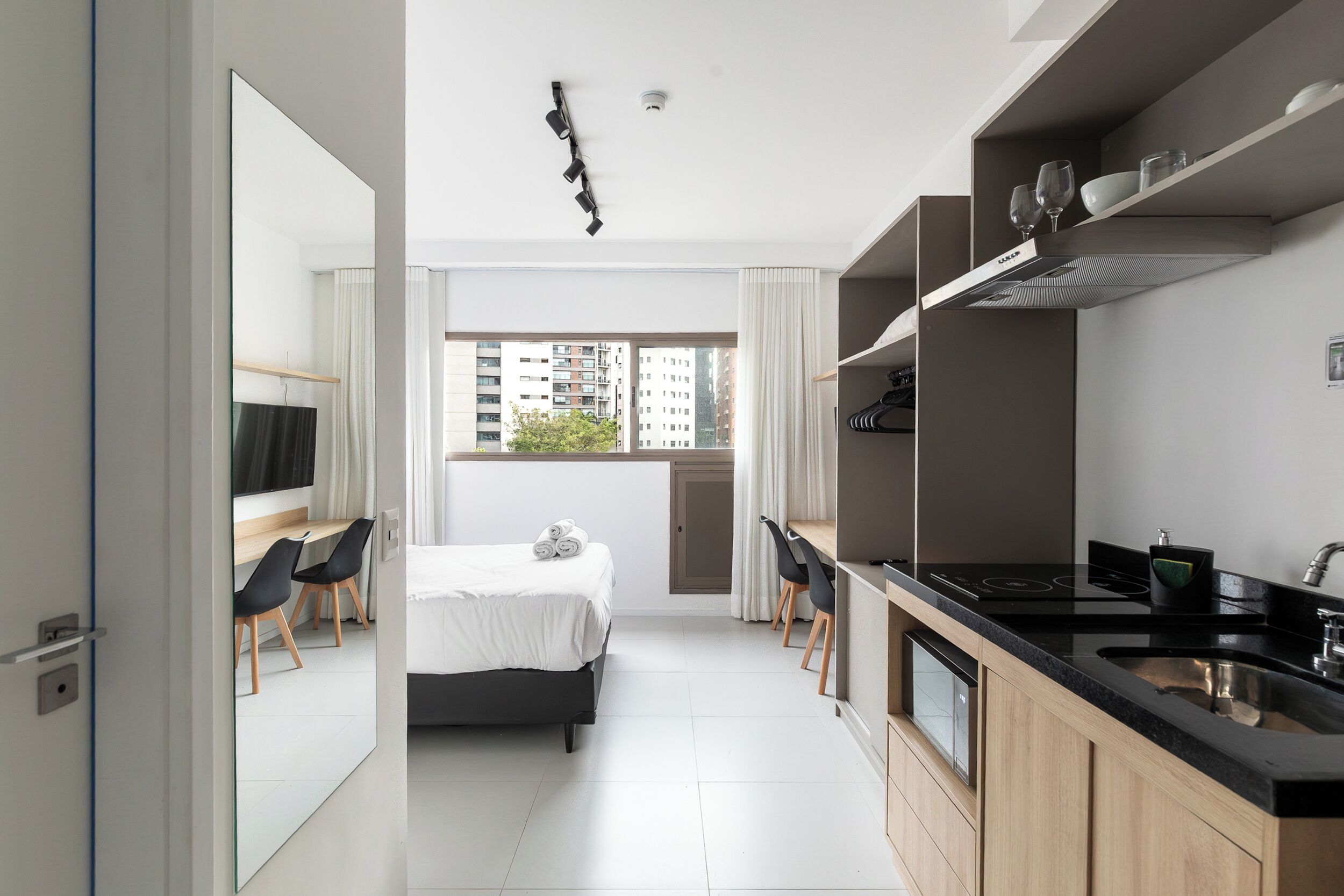 Quarto de hotel moderno com cama, escrivaninha, cozinha compacta e vista para a cidade.