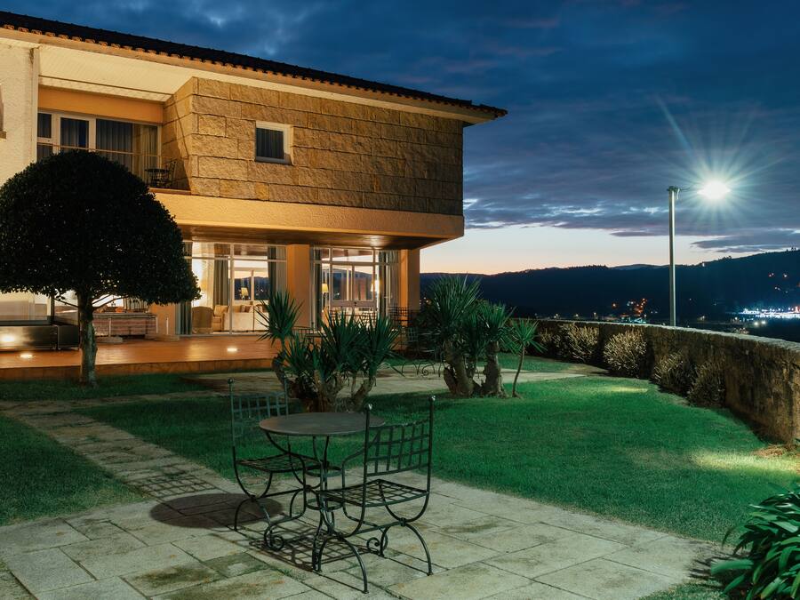 Uma casa de dois andares com fachada de pedra, varanda e um pátio bem iluminado com mesa e cadeiras.