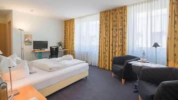 Quarto de hotel com cama, escrivaninha, cadeira, televisão e cortinas.