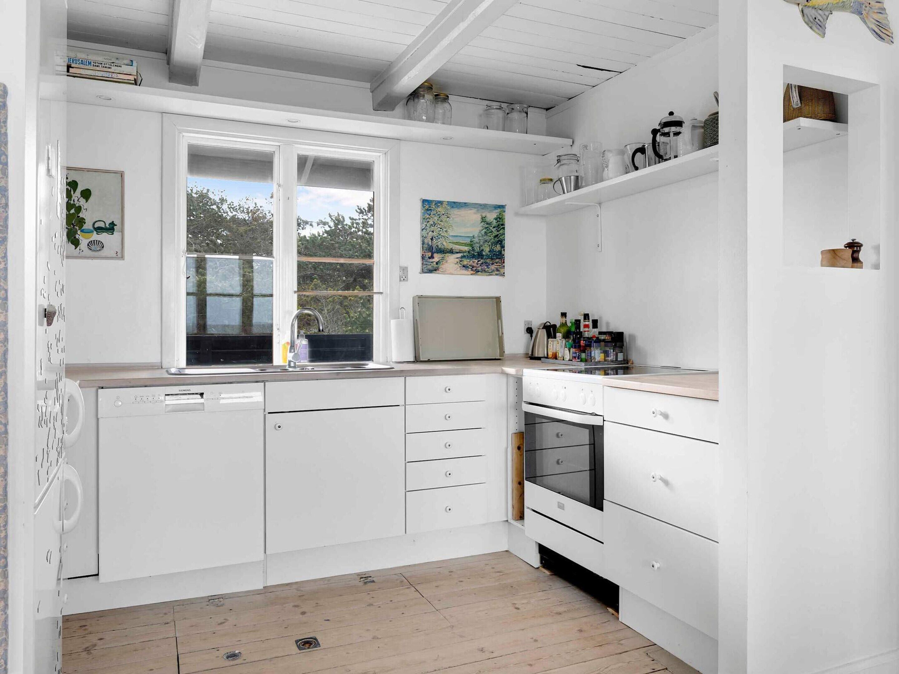 Uma cozinha moderna com armários brancos, lava-louças, forno e janela com vista para um jardim.