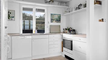 Uma cozinha moderna com armários brancos, lava-louças, forno e janela com vista para um jardim.
