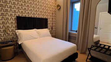 Quarto moderno com teto de madeira, parede estampada, cama com roupa de cama branca, mesa de cabeceira e janela com cortinas.