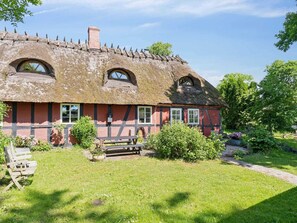 Uma casa tradicional com telhado de palha e um jardim em frente.