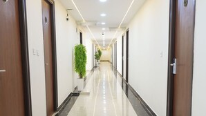 Corredor longo e bem iluminado, com piso de mármore, portas de madeira e plantas em vasos.