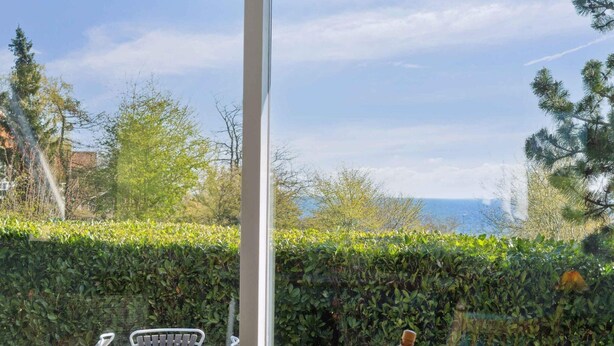 Quarto com uma grande janela com vista para um jardim ajardinado e para o mar.