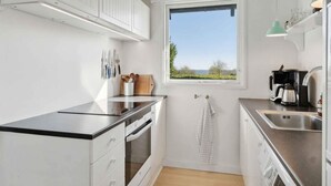 Uma cozinha compacta com armários brancos, forno embutido, pia e janela com vista para o exterior.