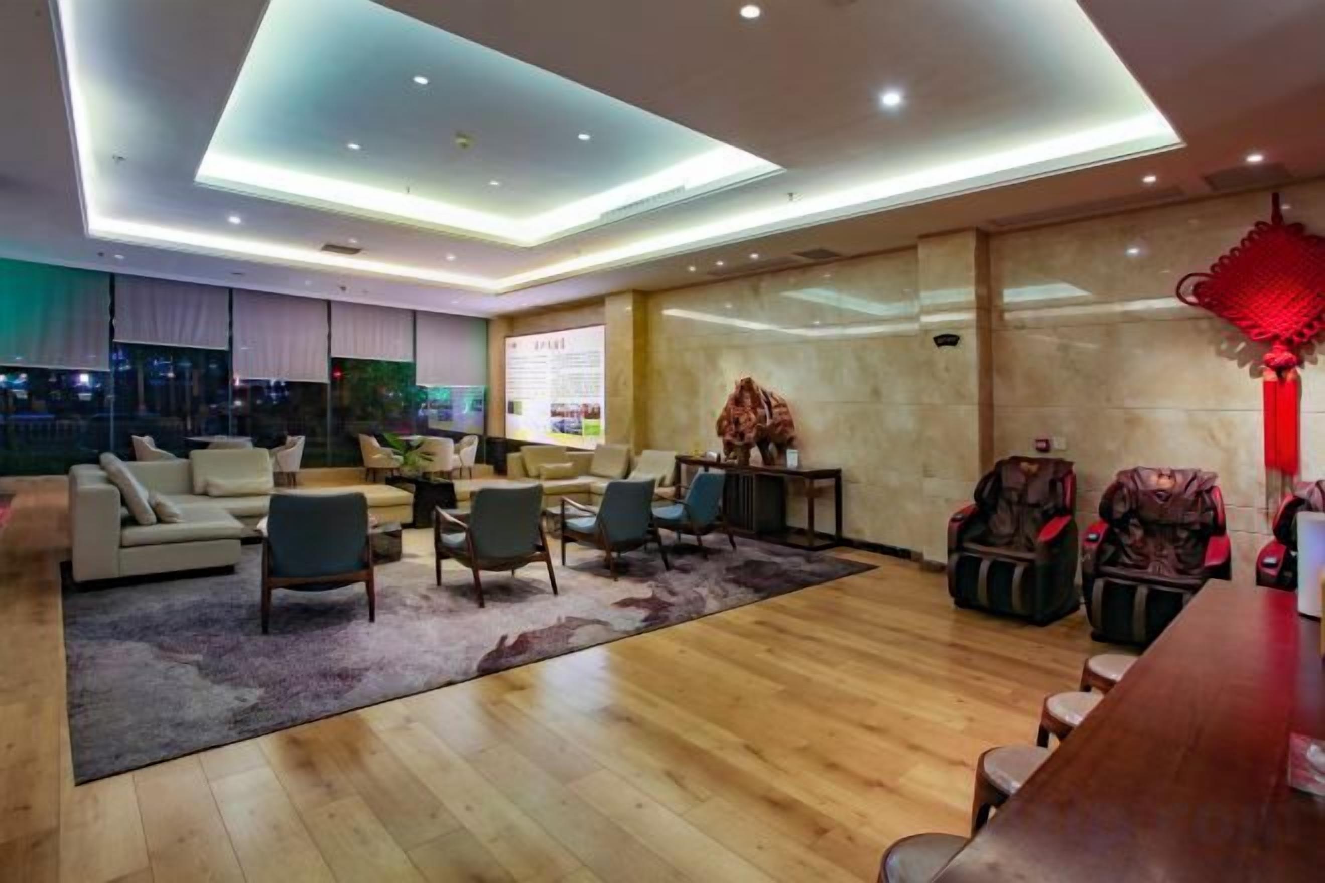 Um saguão de hotel moderno com área de estar, balcão de recepção e uma tela grande exibindo informações.