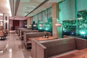 Um hall de hotel com áreas de estar, balcão de recepção e uma grande janela com vista para o verde.