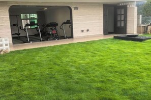 Uma casa com gramado bem cuidado, uma garagem com equipamentos de exercícios e uma porta dando acesso à garagem.