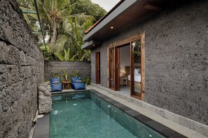 Uma área de piscina com muro de pedra, um espaço de estar pequeno com almofadas e um deck de madeira.