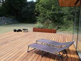Um deck de madeira com duas cadeiras reclináveis, uma mesa pequena e um vaso de plantas.