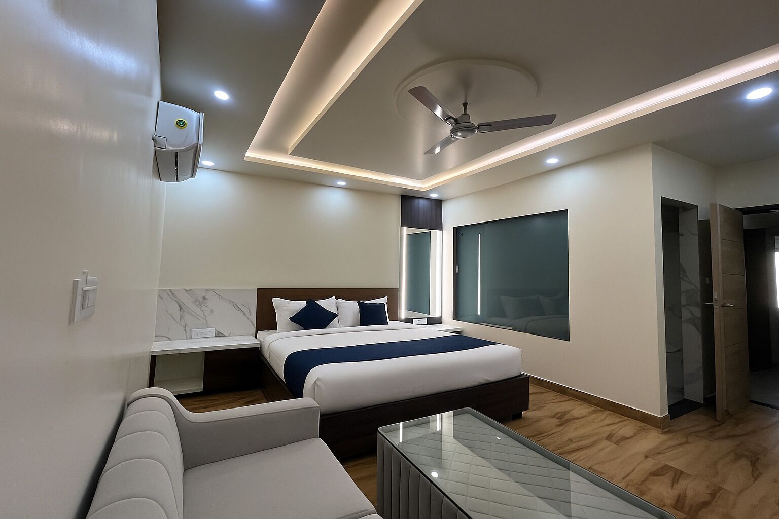 Quarto de hotel moderno com cama, mesa de cabeceira e uma mesa de centro de vidro.