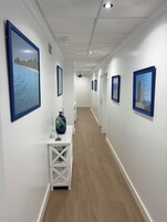 Um corredor com quadros nas paredes, um console branco com um vaso e piso de madeira.