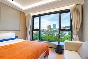 Quarto de hotel com uma janela grande, uma cama, uma cadeira e uma mesinha.