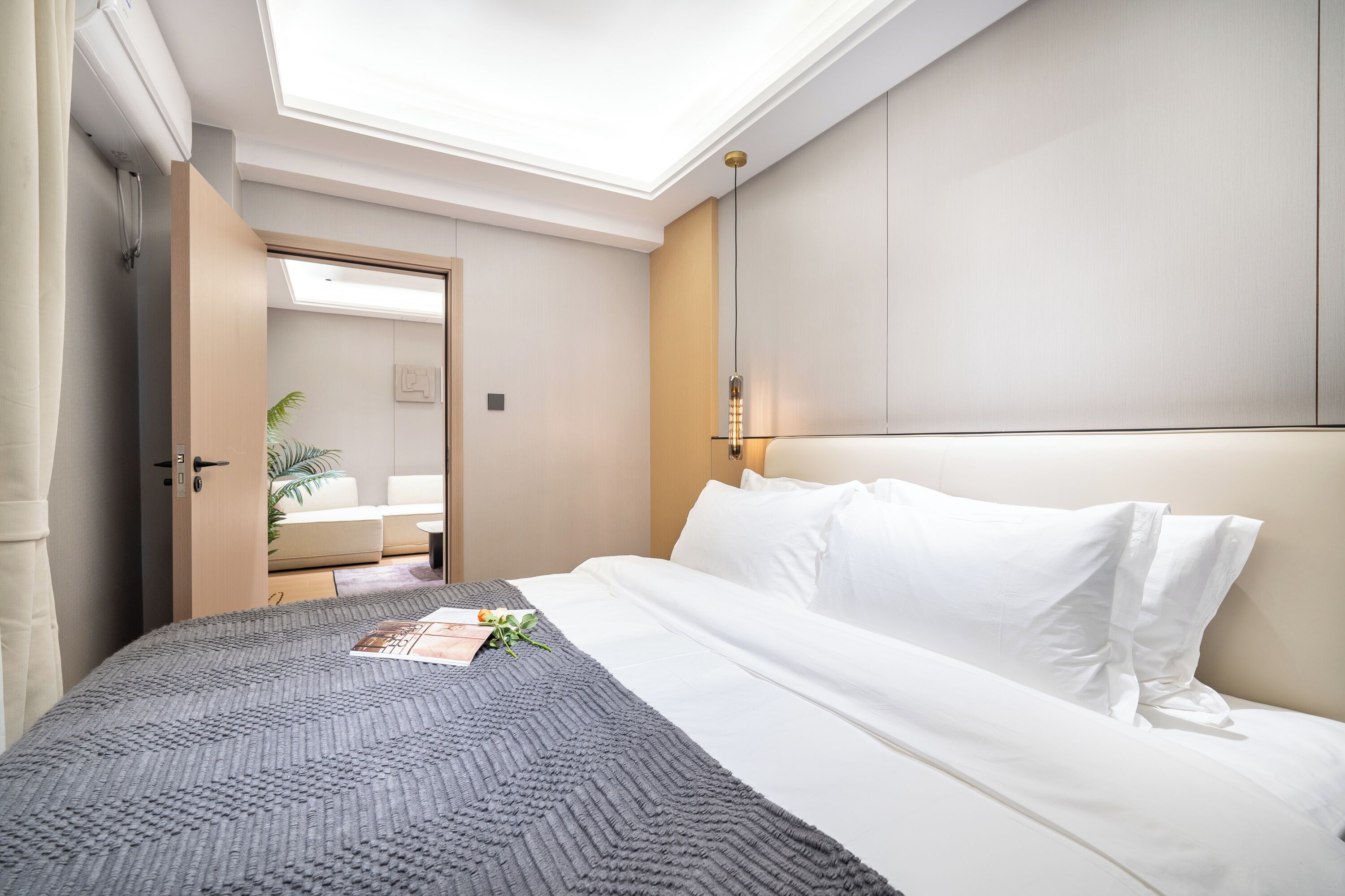 Quarto de hotel com uma cama grande, uma mesa de cabeceira, luminária fixada na parede e porta para um banheiro.