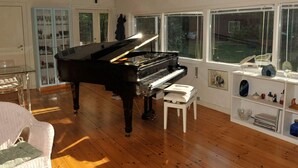 Quarto espaçoso com um piano de cauda, piso de madeira, mesa de vidro e poltrona branca.