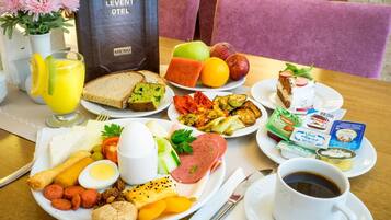 Buffet de café da manhã com diversos alimentos, um suporte para cardápio e uma xícara de café sobre a mesa.